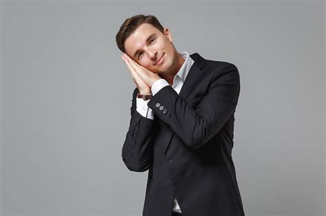 회색 벽 배경에 고립 포즈 고전적인 검은 정장 셔츠에 젊은 사업가 를 미소 성취 경력 재산 사업 개념 복사 공간을 모의합니다 뺨 아래 접힌 손으로 잠을 자 20 29세에