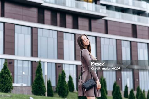 그녀의 어깨에 검은 핸드백드레스에 사무실 건물의 배경에 좋은 분위기의 젊고 아름다운 소녀 건물 근처에는 아름다운 녹색 잔디밭이