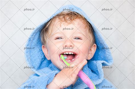 عکس با کیفیت کودک زیبا با چشم های آبی و حوله آبی تنش در حال مسواک زدن