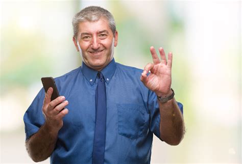 손가락 우수한 기호 확인 서명 하 고 격리 된 배경 위에 스마트폰을 사용 하 여 메시지를 보내는 잘생긴 수석 남자 문자 메시지 개념에 대한 스톡 사진 및 기타 이미지