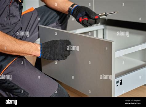 Man Assembling Kitchen Drawer In Modern Cabinet Using Screwdriver