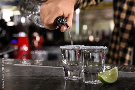 Bartender Pouring Mexican Tequila Into Shot Glasses At Bar Counter