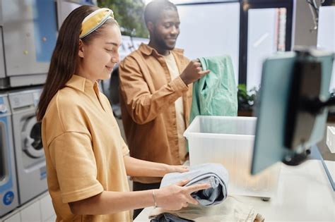 Vista Lateral De Una Mujer Joven Sonriente Doblando Ropa Limpia Y Seca