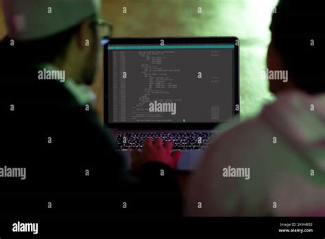 Back View Of Two Diverse Male Colleagues Using Laptop With Coding On