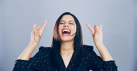 미친 비명을 지르고 회색 배경에 표현 또는 공간을 위해 스튜디오에서 바위 손 제스처를 가진 여자 문화 날카로운 여성 로커와 악마의 뿔 기호 펑키 이모티콘 및 펑크 기호가있는