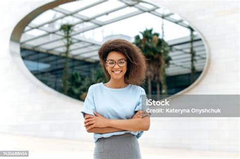 자신감 넘치는 성공적인 아프리카 계 미국인 곱슬 비즈니스 여성의 초상화 우아한 세련된 옷 안경 교차 된 팔로 비즈니스 센터 근처 야외에 서서 카메라를보고 미소 짓는다 20