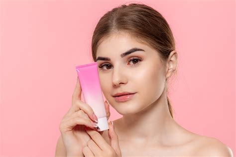 피부를 촉촉하게하는 크림튜브를 들고 있는 아름다운 소녀 모델은 분홍색 배경 위에 격리 된 카메라를 봅니다 미용 및 건강 치료의 개념 갈색 머리에 대한 스톡 사진 및 기타
