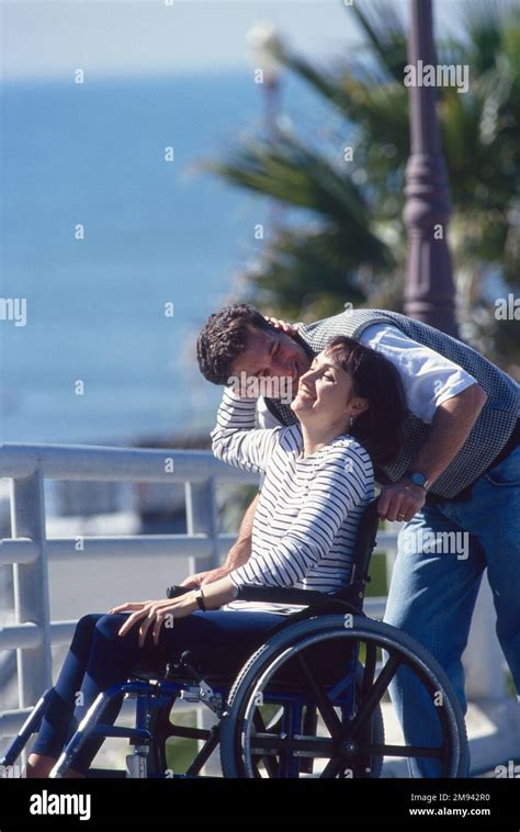 Young Man Pushing A Woman In A Wheelchair Bending Over To Give Her A