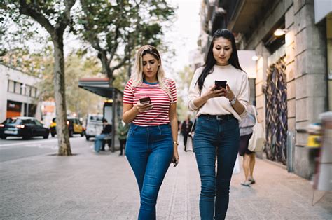 스마트 폰 가제트를 손에 들고 도시 환경에서 걷고 라이브 통신을 무시하는 두 명의 여성 네트워크에서 채팅하는 중독 된 힙스터