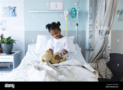 Happy African American Girl Patient Lying On Bed Playing With Teddy