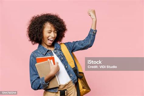 행복한 행운의 작은 아프리카 아이 여학생 1213 세 캐주얼 의류 배낭 에서 책 을 들고 우승자 제스처 Clench 주먹은 파스텔 핑크 배경에 고립 된 축하 어린 시절 교육