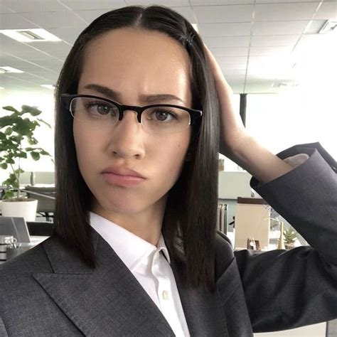 A Woman Wearing Glasses And A Suit In An Office Setting With Her Hand