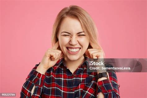 예쁜 여자의 스튜디오 샷 Clenches 치아와 불만으로 불쾌 한 사운드 나 음악을 듣는 귀를 플러그 매력적인 모습 분홍색