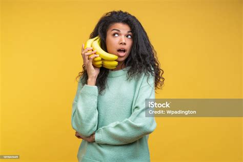 재미 긍정적 인 옷차려 낸 아프로 미국 소녀의 초상화는 노란색 배경에 고립 된 바나나 전화를 통해 전화를 걸고 바나나에 대한