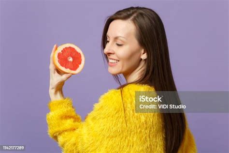 스튜디오에서 보라색 파스텔 벽 배경에 고립 된 신선한 익은 자 몽의 절반 손을 잡고 모피 스웨터에 예쁜 젊은 여자 사람들은 생생한 라이프 스타일 휴식 휴가 개념입니다 복사