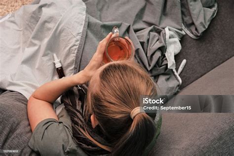 소녀는 집에서 아프다 소파에 앉아 담요에 싸여 목에 스카프를 두르고 있었다 뜨거운 차를 마십니다 위에서 볼 수 있습니다 코로나
