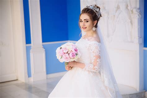 신부 드레스에 밝은 머리와 부드러운 여자 블루 홀에 모란의 꽃다발을 들고 있다 신부는 큰 투명 한 돌으로 만든 왕관과 함께 그녀의 헤어스타일을 장식 결혼식에 대한 스톡 사진