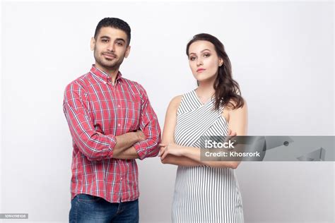 빨간색 체크 무늬 셔츠에 심각한 자랑 잘생긴 남자가 서와 교차 팔 카메라 보고 흰색 스트라이프 드레스에서 아름 다운 여자의 초상화 2명에 대한 스톡 사진 및 기타 이미지