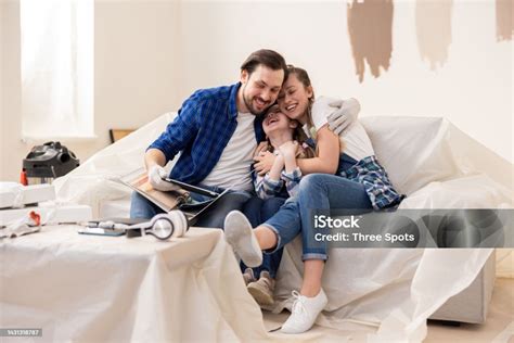 하얀 티셔츠 파란색 청바지 체크 무늬 셔츠를 입은 중년의 갈색 머리 남자가 아름다운 아내와 8 살짜리 귀여운 딸을 포옹합니다 가족은 집에서 수리를 시작했기 때문에 정말