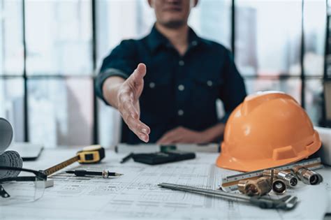 엔지니어링은 사무실 책상과 계산기 삼각형 눈금자 안전 안경 나침반 블루프린트의 버니어 캘리퍼에서 도면 검사와 좋은 거래로 작업한 후 악수를 하고 싶어합니다 엔지니어 건축가