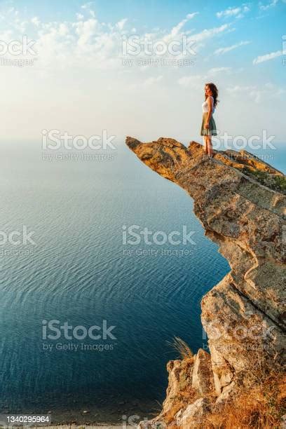 한 젊은 여성이 하늘에 맞서 바다 위의 그림 같은 가파른 절벽에 서 있습니다 여행과 자유의 개념 가파른에 대한 스톡 사진 및