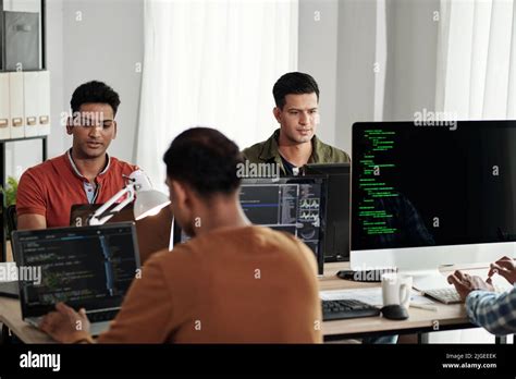Group Of Young Indian Devops Engineers Working In Modern Office Coding