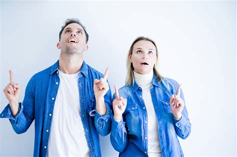 孤立した白い背景の上に立っているデニムシャツを着た若い美しいカップルは驚き指と腕で上を向いて驚きました 2人のストックフォトや画像を多数ご
