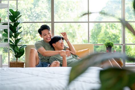 두 명의 게이 또는 Lgbt 남자는 포옹을 즐기고 행복한 감정으로 서로를 놀리고 낮 빛이있는 침실의 침대 근처의 소파에 앉아