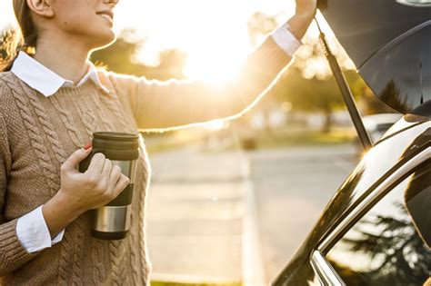 젊은 여자는 주차장 주차장에 서서 차 옆에서 보온병에서 커피 한 잔을 즐기고 있다 20 24세에 대한 스톡 사진 및 기타 이미지