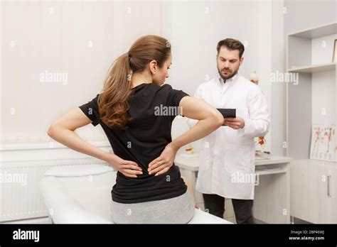 Male Doctor Examining Female Patient Suffering From Back Pain Medical