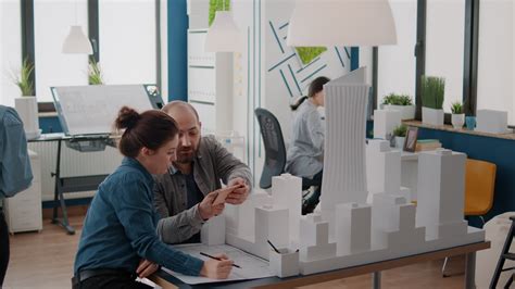 Colleagues Using Smartphone To Analyze Building Model And Blueprints
