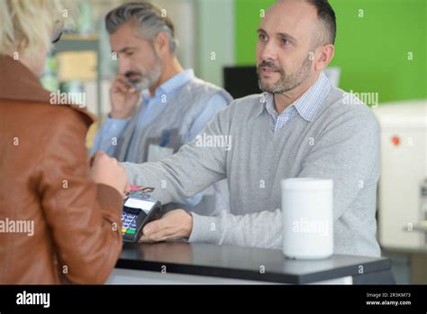 Sales Clerk Passing Card Reader To Customer For Entering Code Stock