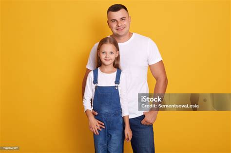 노란 배경 위에 고립 된 그녀의 잘 생긴 아버지와 함께 웃고 서있는 사랑스러운 딸의 초상화 캐주얼 한 옷을 입은 가족 카메라를 직접 보고 깊은 헌신과 관계 가족에 대한 스톡