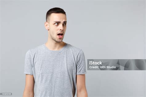 캐주얼에 충격 젊은 남자의 초상화 옆을 찾고 서 서 스튜디오에서 회색 벽 배경에 고립 된 입을 열어 유지 사람들은 진심으로 감정
