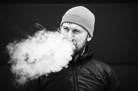 Vape 남자입니다 젊은 흰 수염 뚜껑에 사람이 전자 담배를 흡연 하 고는 증기 시키는 나쁜 습관입니다 흑인과 백인입니다 가을에