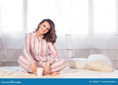 Девушка в пижамах сидя на кровати с чашкой Стоковое Изображение изображение насчитывающей
