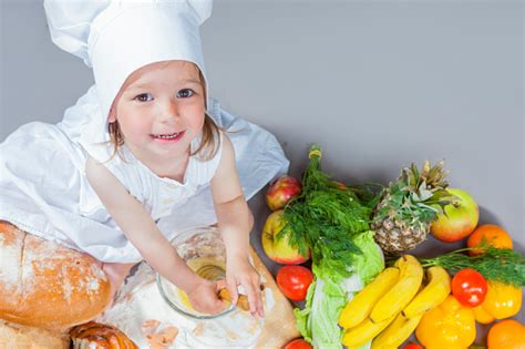 요리 아이디어 스튜디오 환경에서 거품기와 주방 유리 제품으로 작업 하는 요리 유니폼에서 백인 어린 소녀 배경에 야채와 과일높은 각도보기 수평 이미지 2 3 살에 대한 스톡