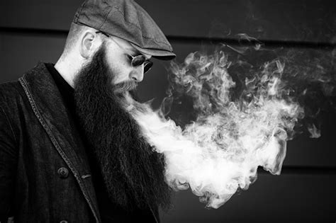 Vape 수염 남자 모자와 선글라스에 아주 긴 수염을 가진 성인 남자 외부 화창한 날에 전자 담배를 피우는 나쁜 습관 흑백