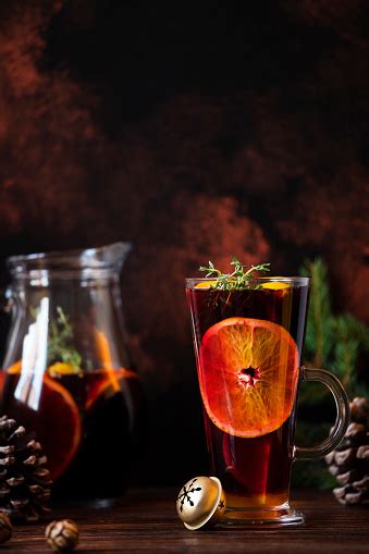 멀드 와인은 크리스마스 장식이있는 나무 테이블에 레드 와인 시트러스 및 향신료로 만든 따뜻한 음료 멀드 와인을 곁들인 유리와 디켄터 어두운 배경 클로즈업 다채로운 카피