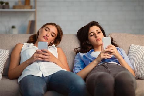 Premium Photo Two Girls Using Smartphones Sitting On Couch Indoor