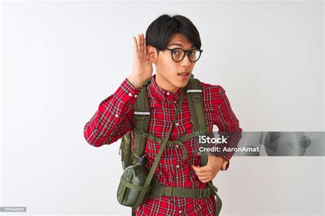 배낭 매통 안경을 쓰고 고립된 흰색 배경 위에 미소를 짓는 중국 등산객 남성이 소문이나 험담에 귀를 기울이며 귀를 기울이고 있습니다 청각 장애 개념입니다 귀 부분에 대한