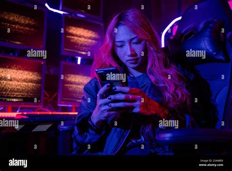 Asian Woman In Front Of A Computer Monitor Display Using Mobile Phone Neon Light Hacker Wear