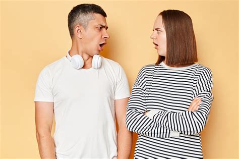 놀란 여자와 남자는 충격에 휩싸여 서로를 바라보고 속보를 듣고 당혹스러워하고 베이지색 배경에 고립된 캐주얼한 옷을 입은 그들의 눈을 믿을 수 없다 2명에 대한 스톡 사진 및