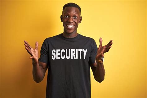 고립된 노란색 배경 위에 보안 유니폼을 입은 아프리카계 미국인 세이프가드 남자는 미친 듯이 축하하고 팔을 들고 눈을 뜨고 흥분을 일으키며 성공을 축하하고 놀랐습니다 우승자