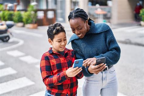 Madre E Hijo Afroamericano Sonriendo Confiados Usando Smartphone En La Calle Imagen De Archivo