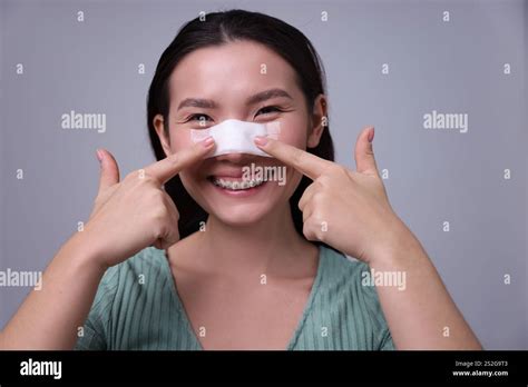 Woman With Medical Bandage On Her Nose After Plastic Surgery Operation Against Light Grey