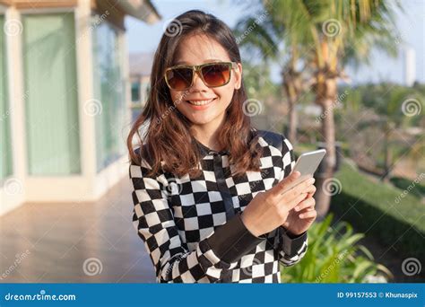 Young Asian Woman Wearing Sun Glasses And Smart Phone In Hand To Stock