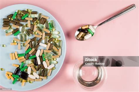 ピンクの背景に多くの栄養補助食品の錠剤コップ一杯の水毎日の丸薬の摂取用のスプーン亜鉛の丸薬老化からの酸化防止剤レシチンとアダプトゲンのセット