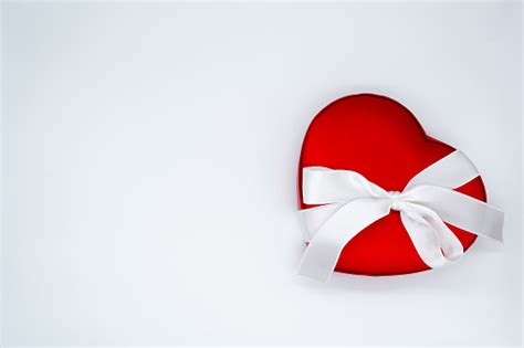 하트 모양의 밝은 빨간 새틴 상자 흰색 배경에 활이달린 흰색 리본으로 묶여 있습니다 사랑의 개념 발렌타인 데이 선물 사랑하는