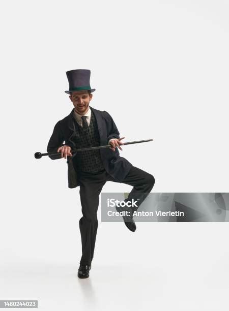 낡은 빈티지 양복과 모자를 쓴 한 신사가 지팡이를 짚고 춤을 추고 흰색 배경 위에 웃고 있다 뼈를 스트레칭 할 시간 16세기 스타일에 대한 스톡 사진 및 기타 이미지